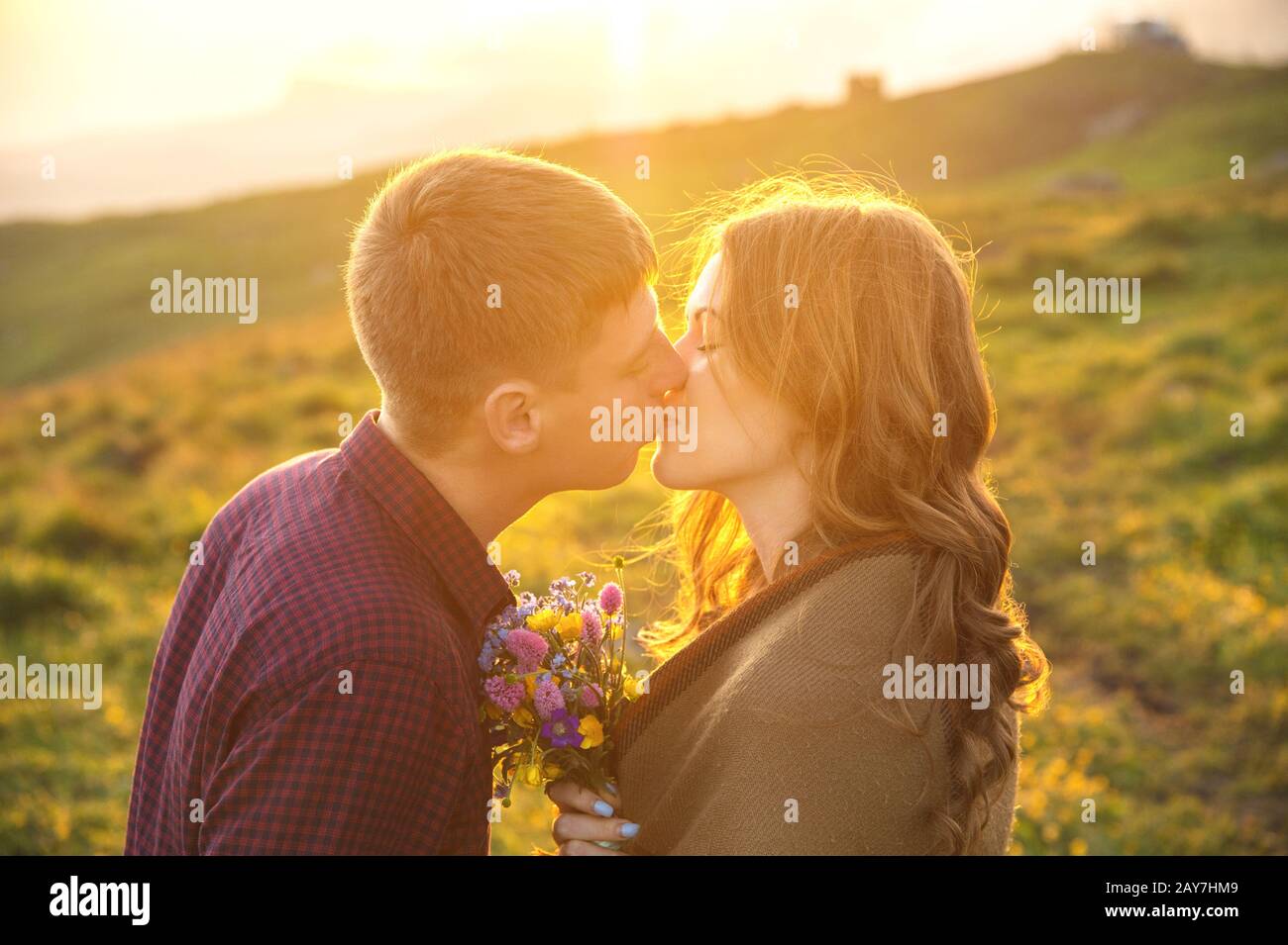 Young happy couple kissing in nature against the setting sun at sunset ...