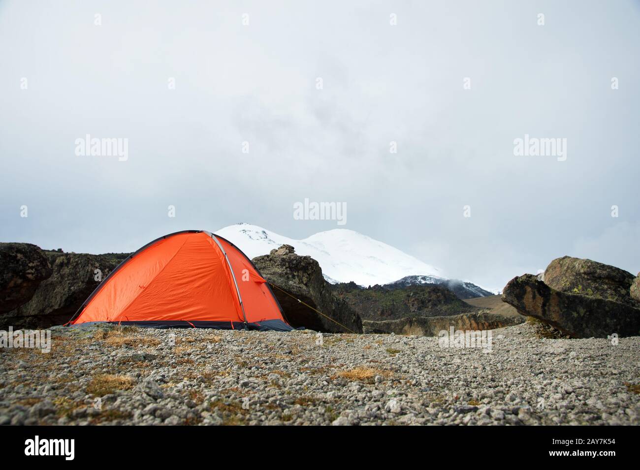An orange high-altitude tent is set high in the mountains against the ...