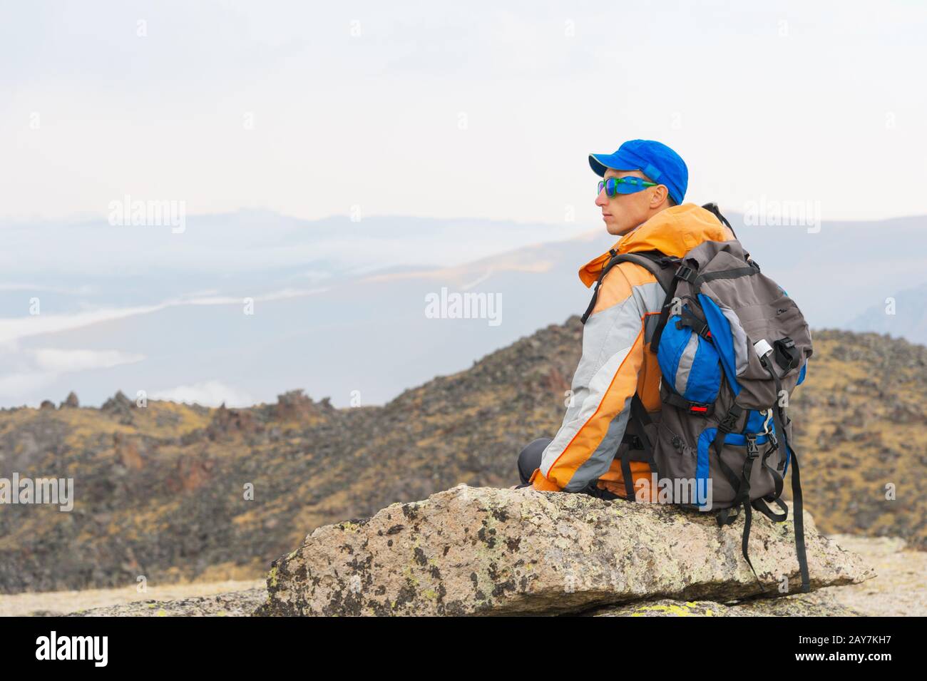 A lonely tourist with a backpack and in sunglasses is resting sitting ...
