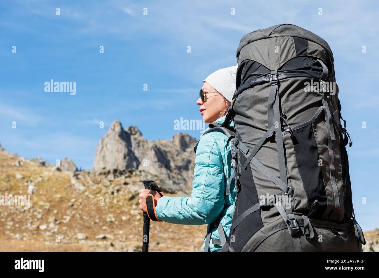 A hiker girl in sunglasses and a hat with a backpack and mountain gear ...