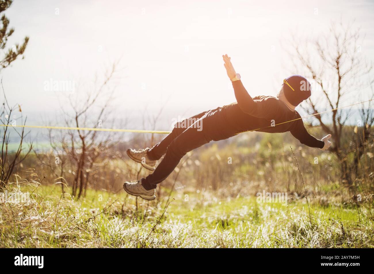 A man with a beard and in sunglasses lying balancing a stretching rope ...