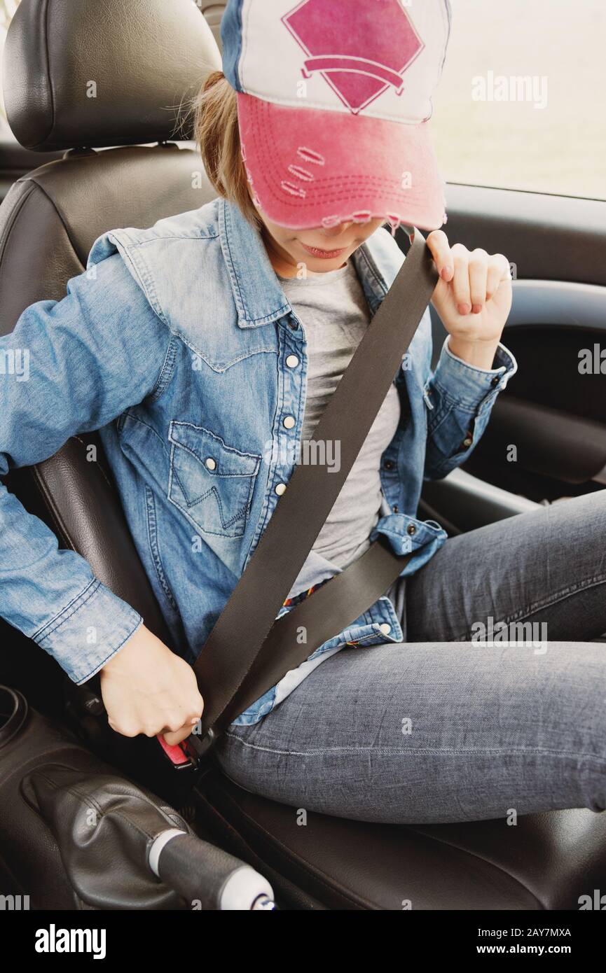 A hipster girl wearing jeans clothes fastens her seat belt in the car ...