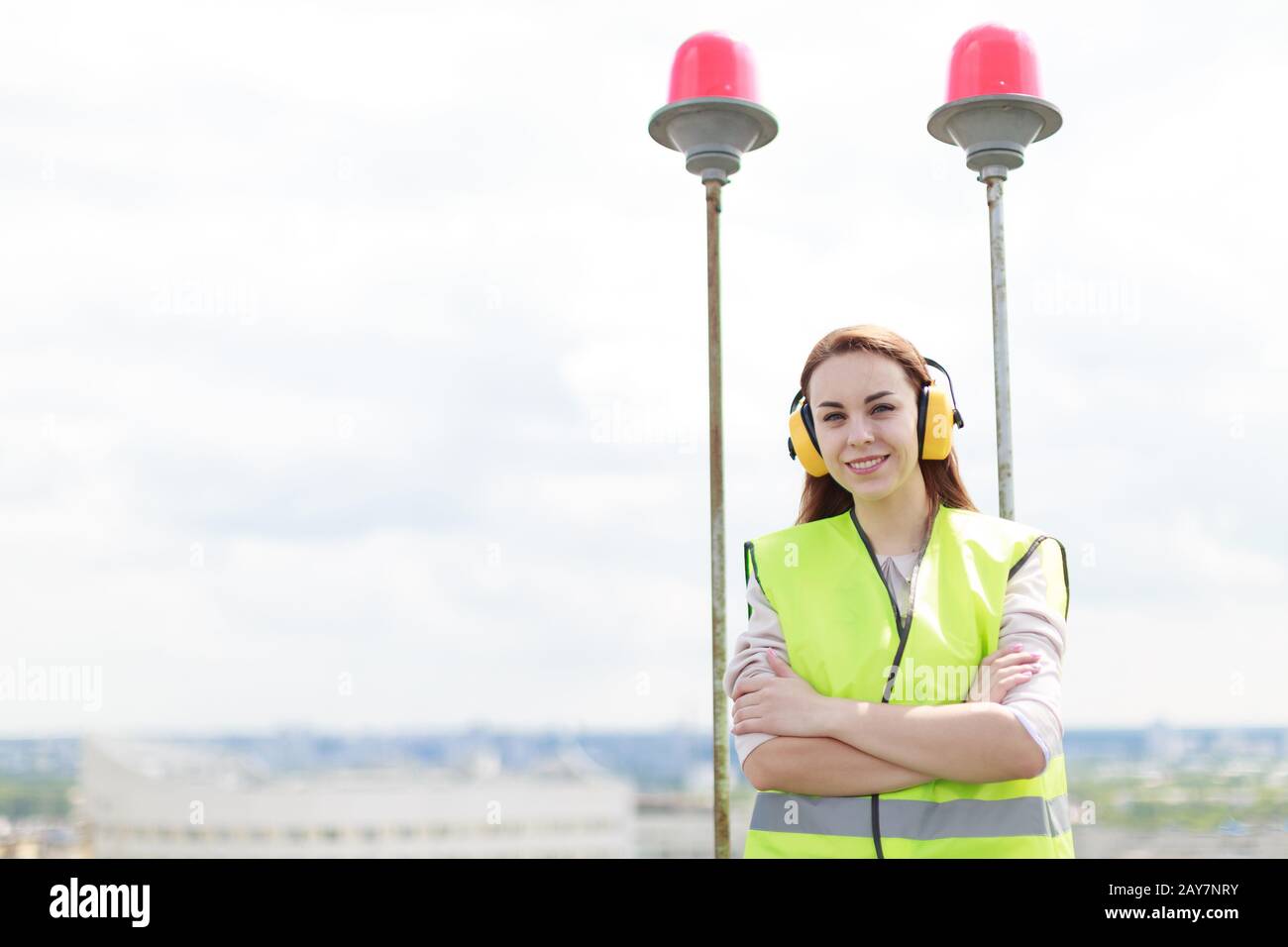 Attractive cute worker woman in green west and earmuffs stand on roof ...