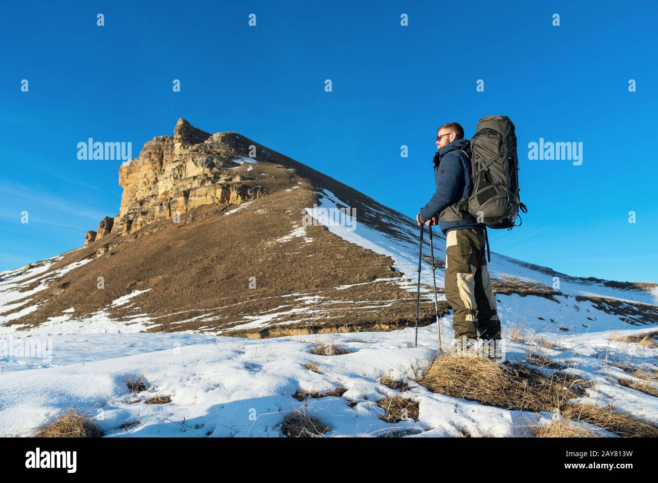 Backpacker with a large backpack and sticks ascends to the rock on ...