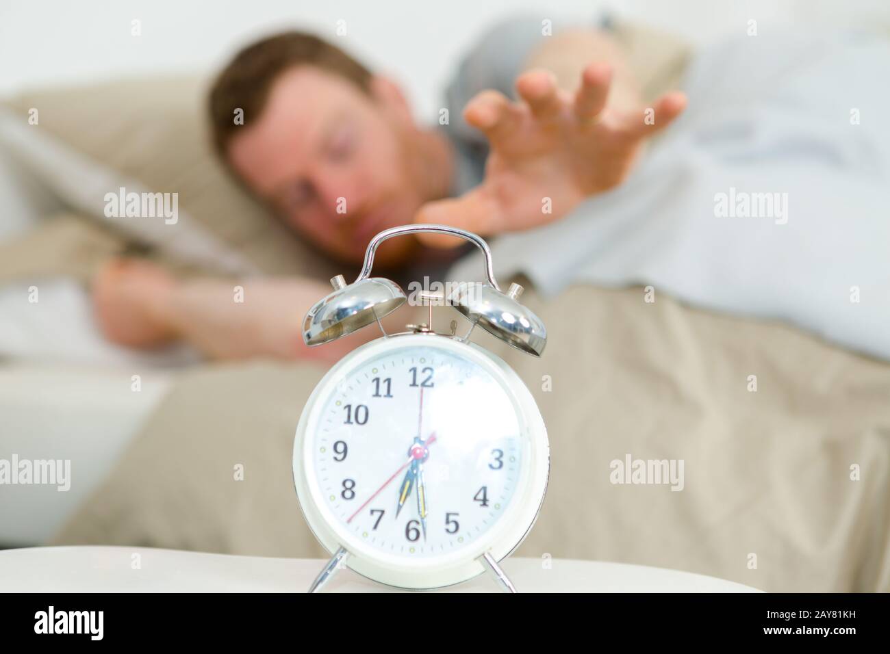 sleepy man reaching to snooze alarm clock Stock Photo - Alamy