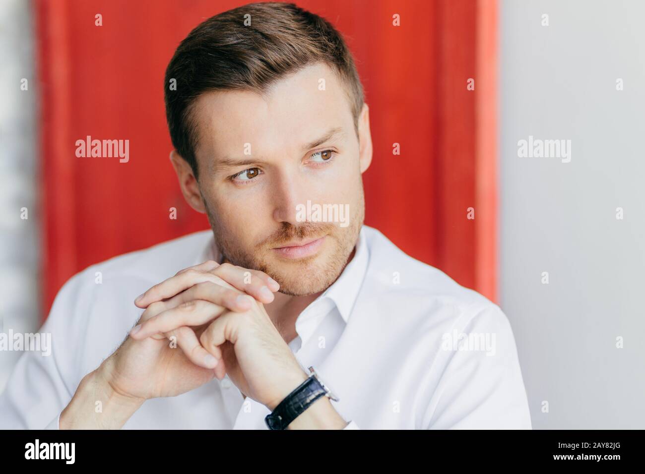 Pensive male director keeps hands presssed together, looks thoughtfully ...