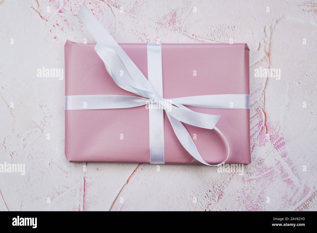 top view on a pink present with white ribbon in the center of a light ...