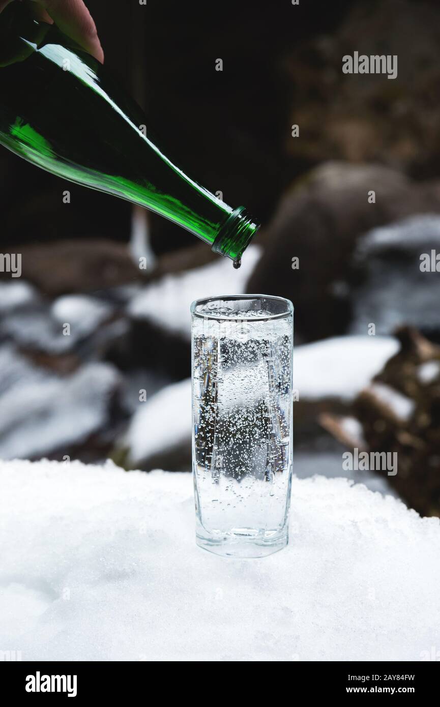 Pure mineral water is poured from a glass green bottle into a clear ...