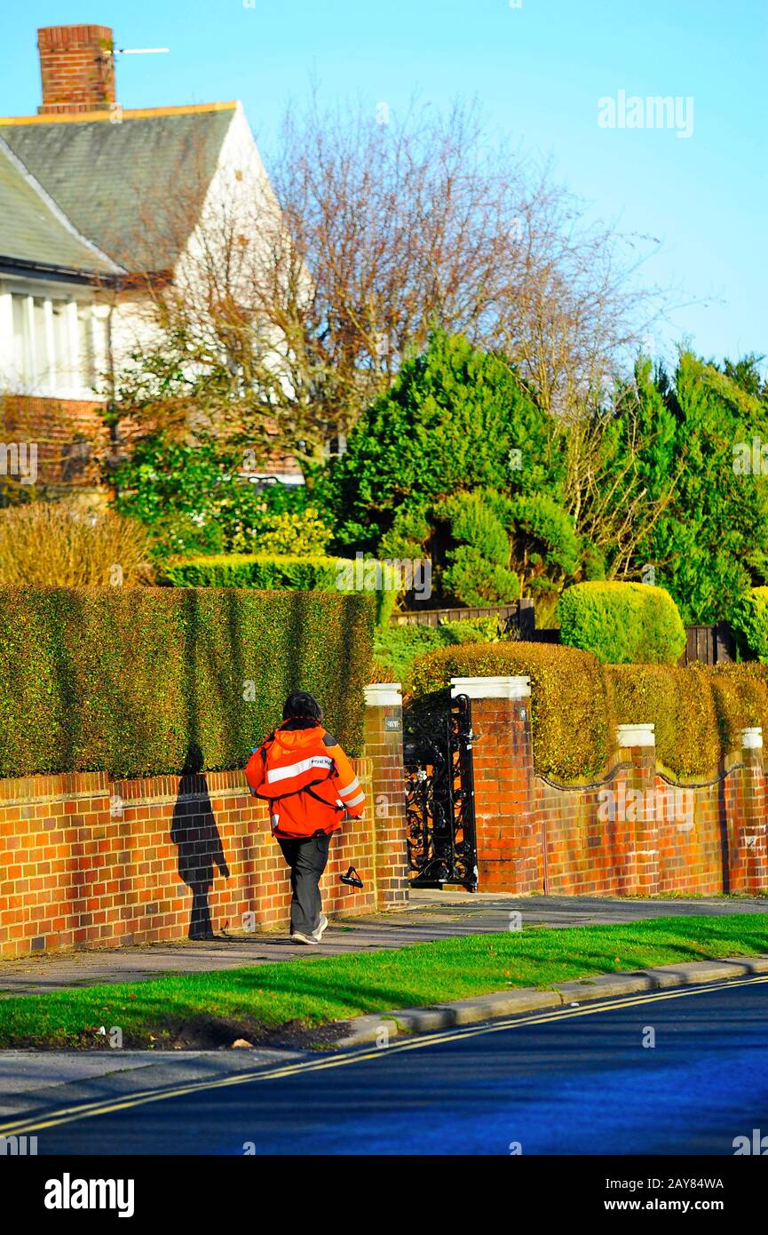 Postman delivering letters on a road containing large detached houses ...