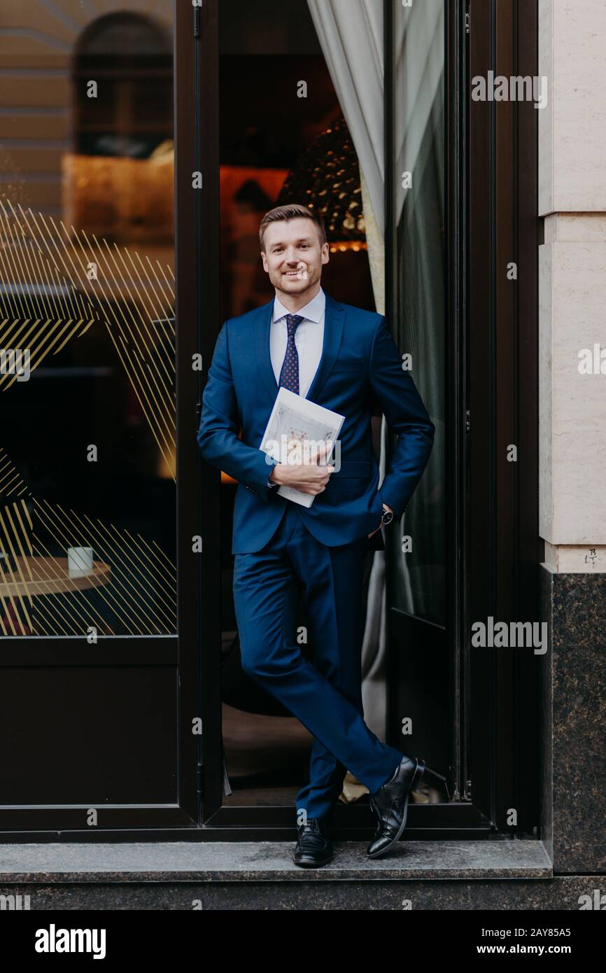 Vertical shot of successful male executive worker in formal suit, keeps ...