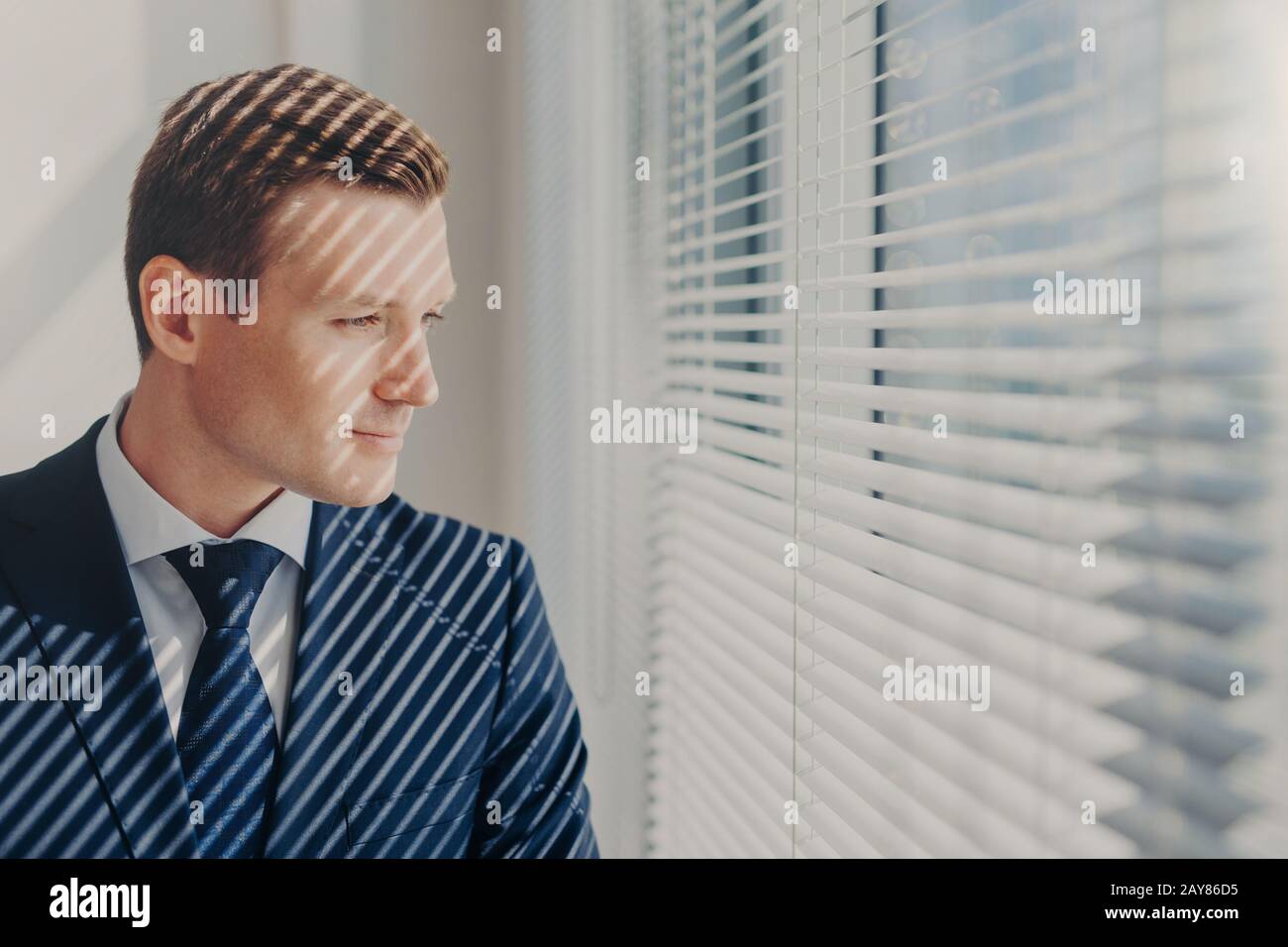 Indoor shot of pensive male economist dressed in formal outfit, looks ...