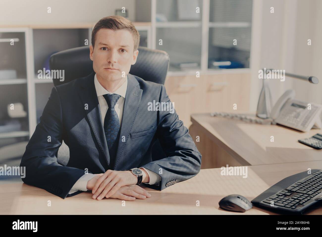 Serious male CEO in formal suit sits at work place in cozy cabinet at ...