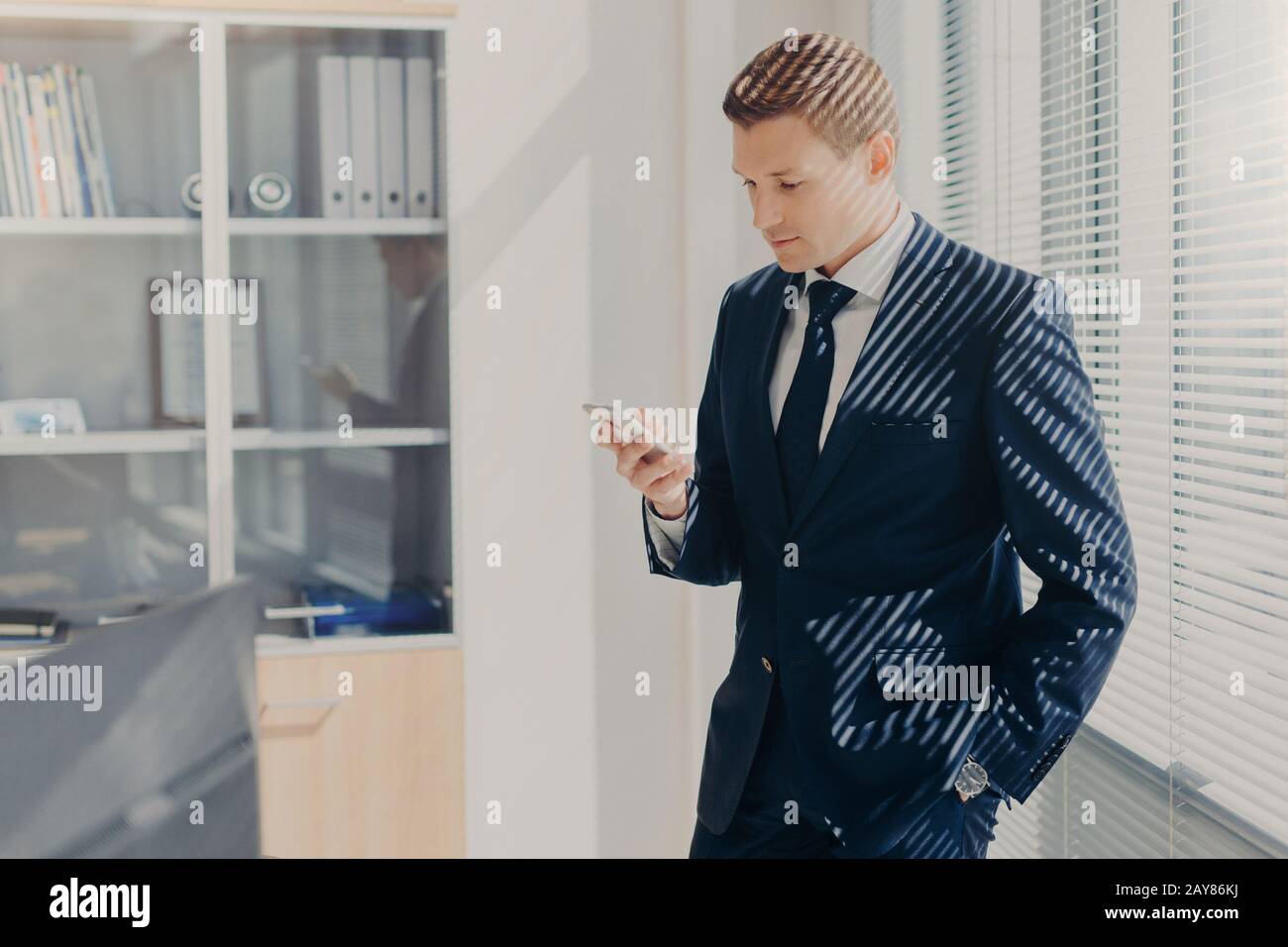 Indoor shot of handsome male business owner, reads text message, stands ...