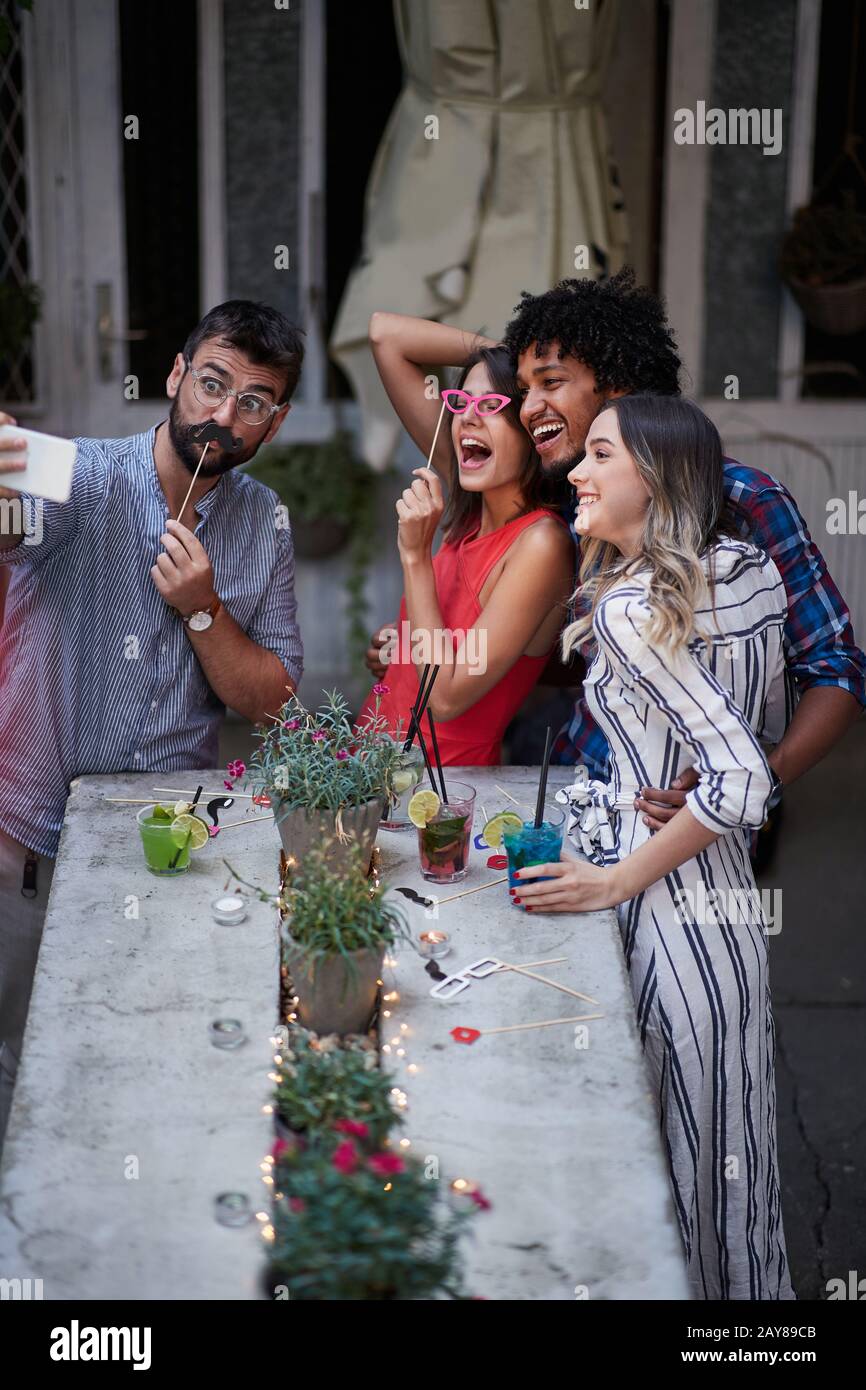 group of four adults having fun at the outdoor bar, taking selfie with ...