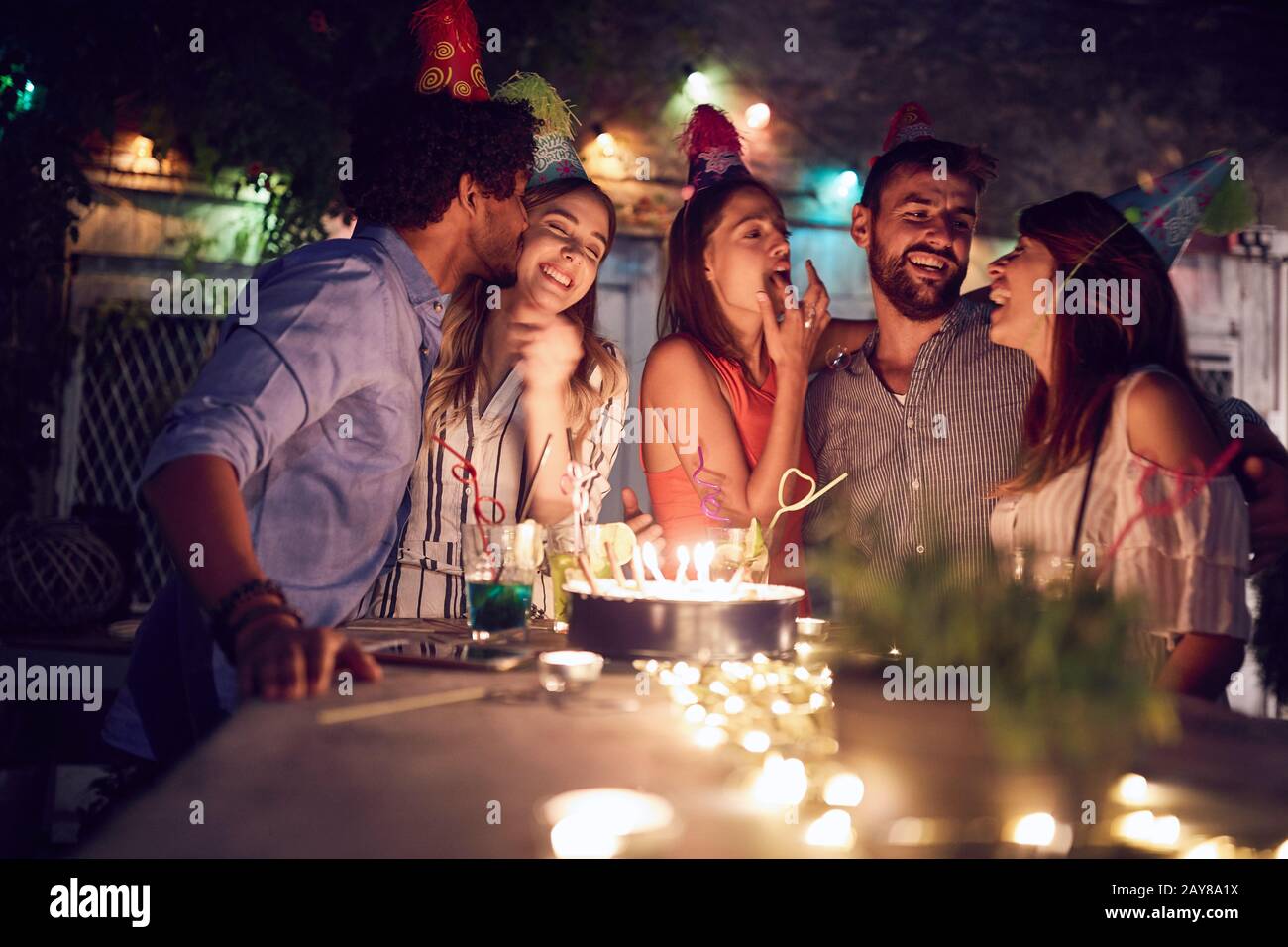 group of young friends celebrating a birthday in the club with cake and ...