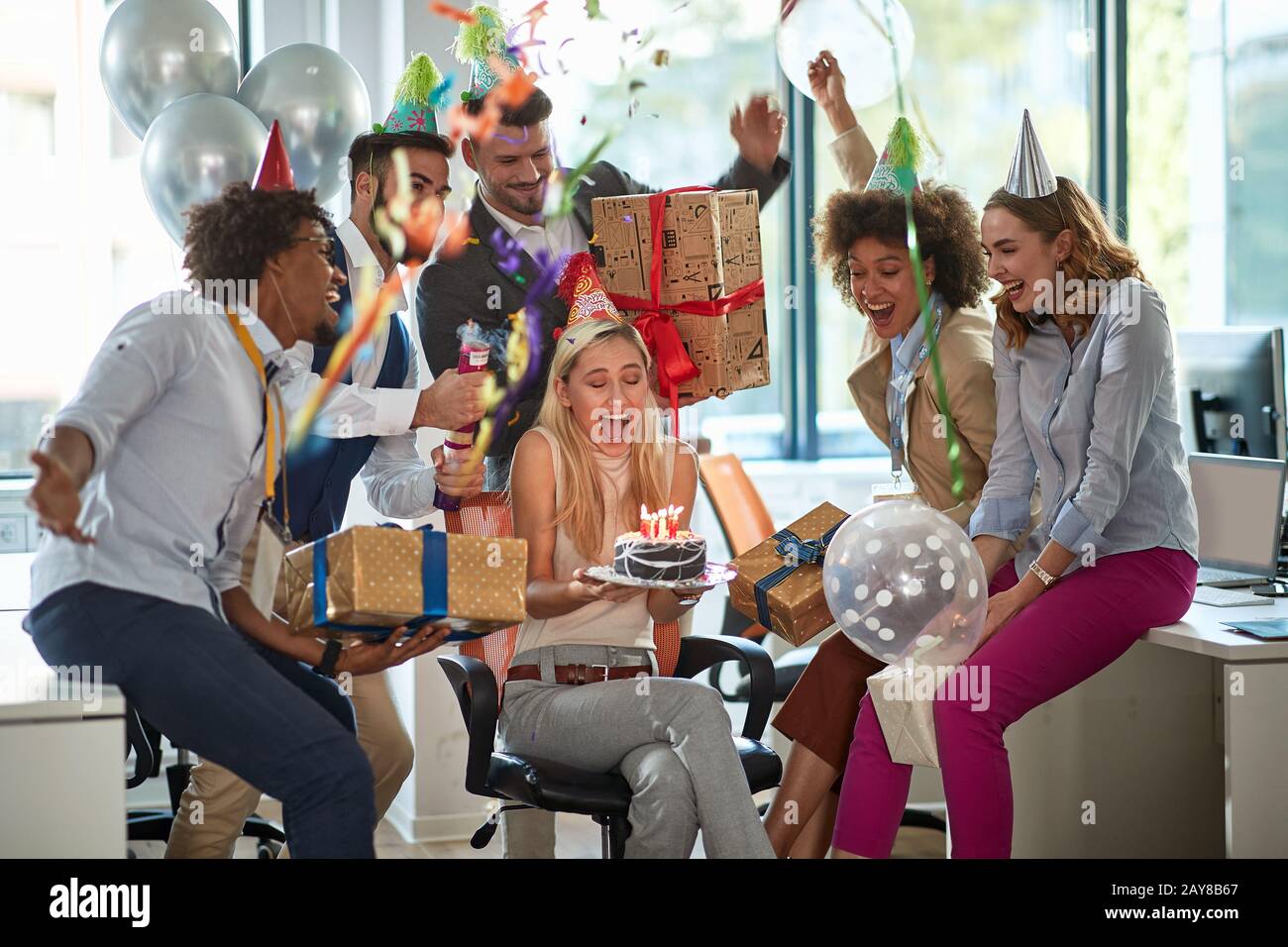 group of colleagues surprising female colleagues with birthday cake and ...