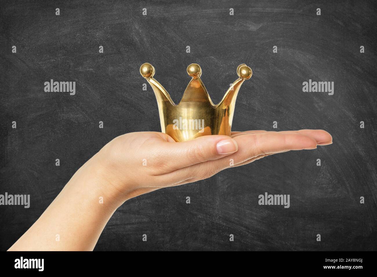 Female hand holding golden crown in front of a chalkboard background ...