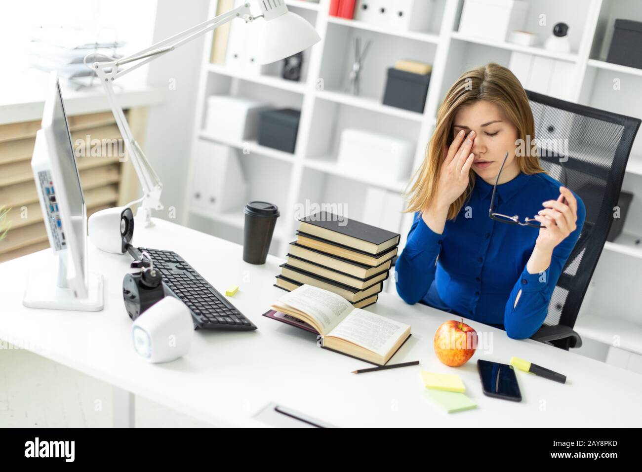 A young girl is sitting at a computer desk, holding glasses in her hand ...