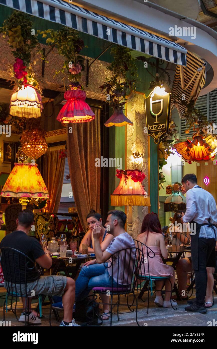 Atmospheric scene of people sitting at an Athens cafeteria late on a ...