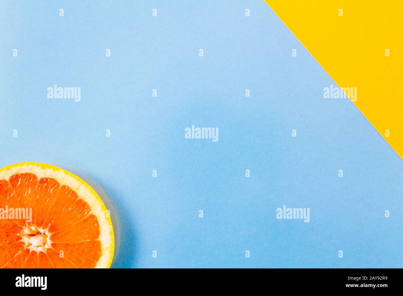 Single grapefruit slice close-up on blue and diagonal yellow background ...