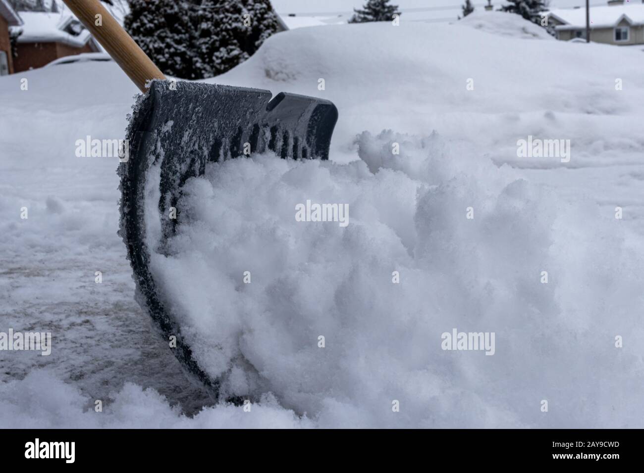 A snow shovel is pushing snow along a suburban driveway in the winter ...