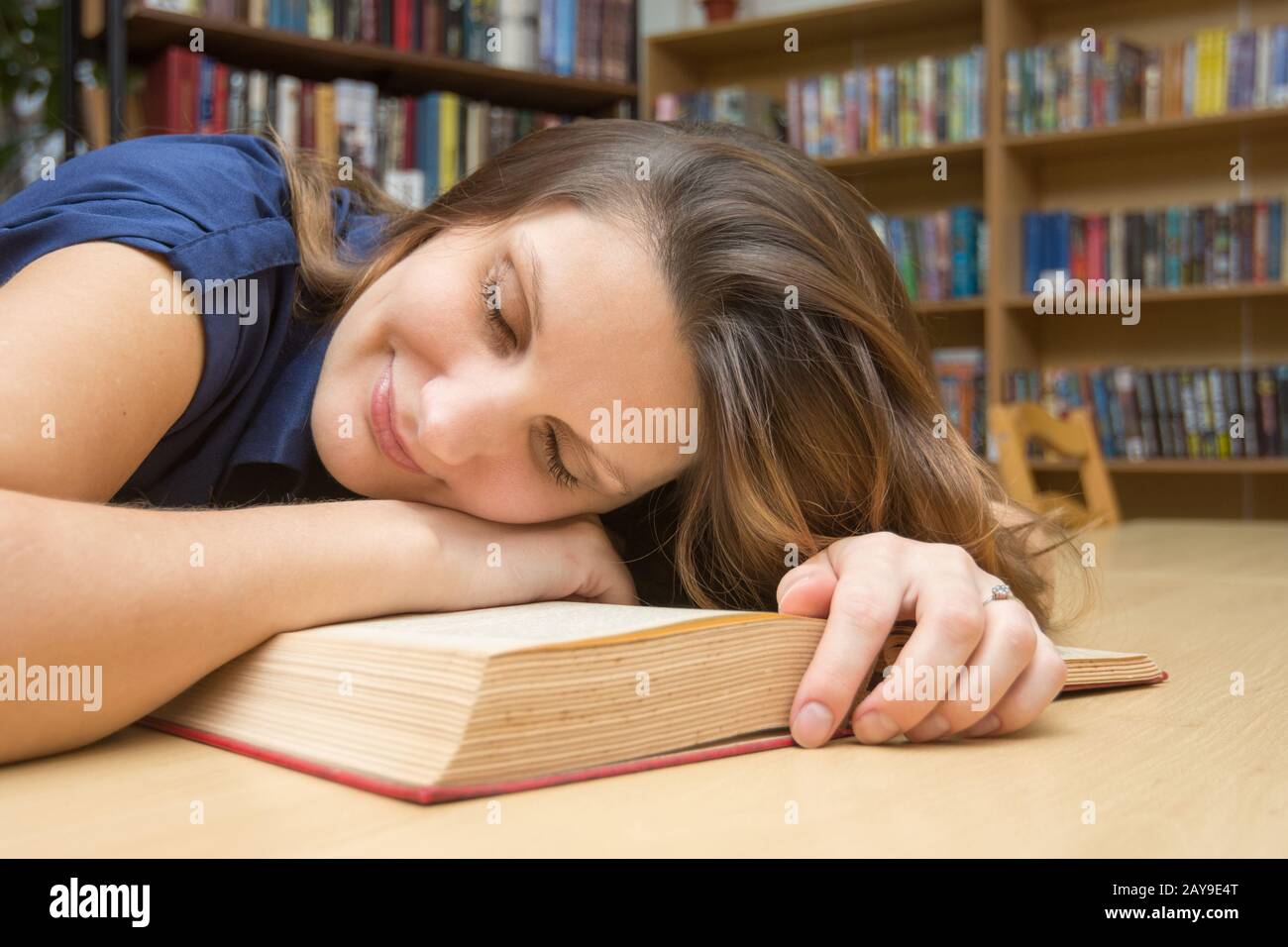 The girl lay down on a book in the library and smiles having closed her ...