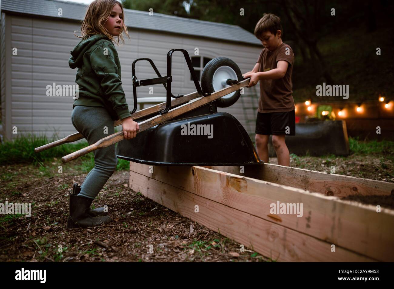 Siblings work together on raised garden bed with soil from wheelbarrow ...