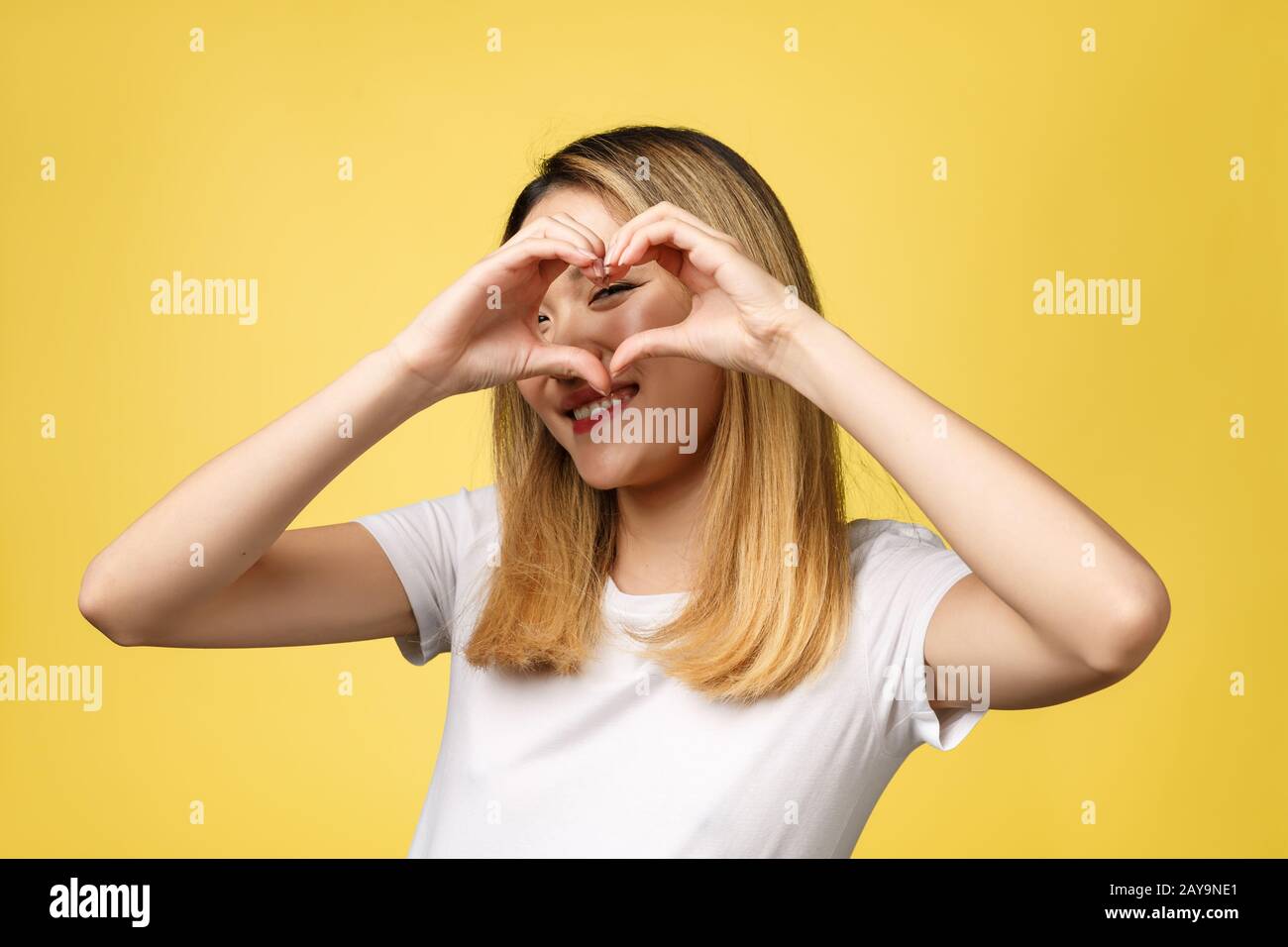 Young Asian woman show heart hand sign isolated on yellow background ...