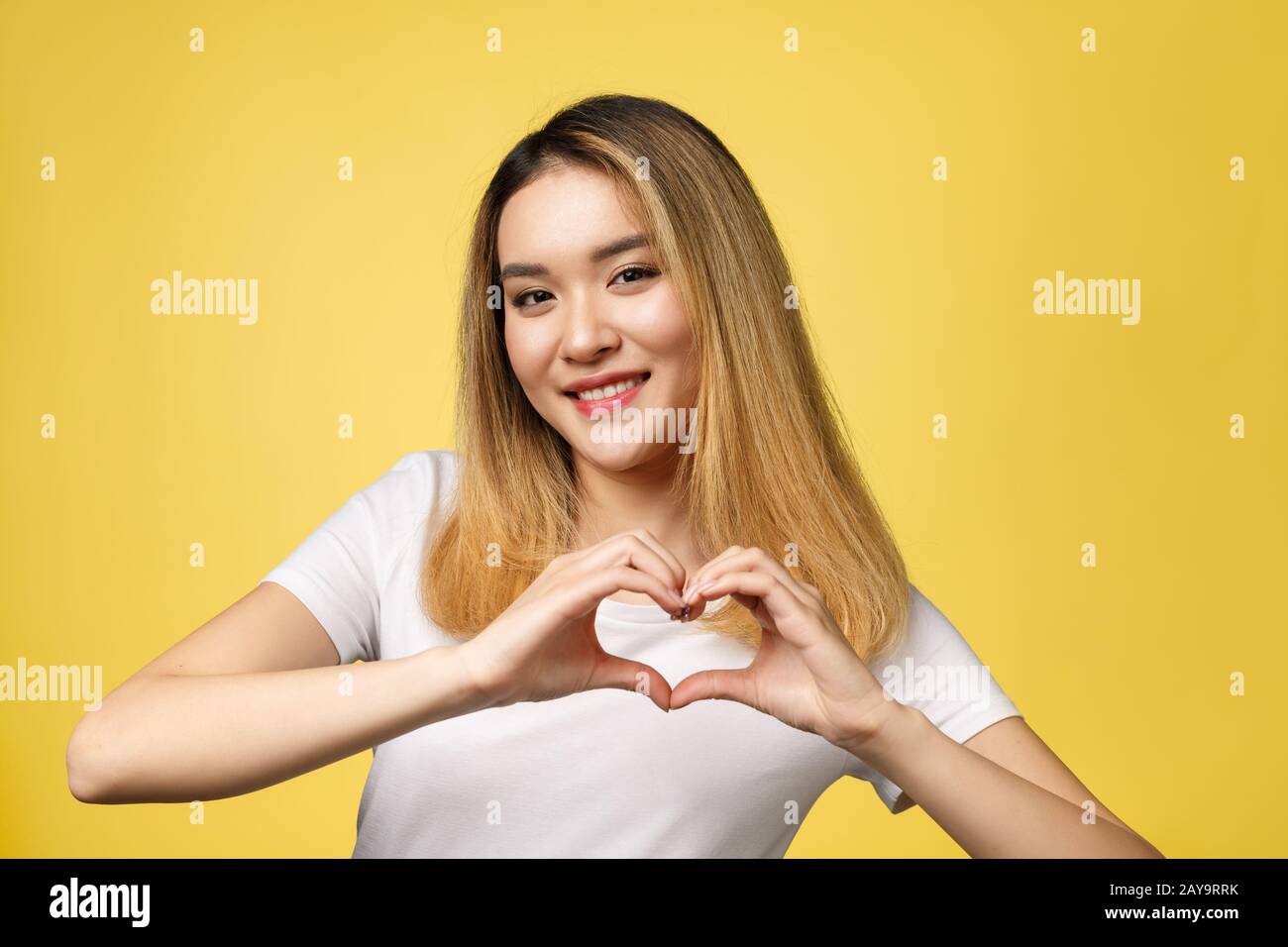 Young Asian woman show heart hand sign isolated on yellow background ...