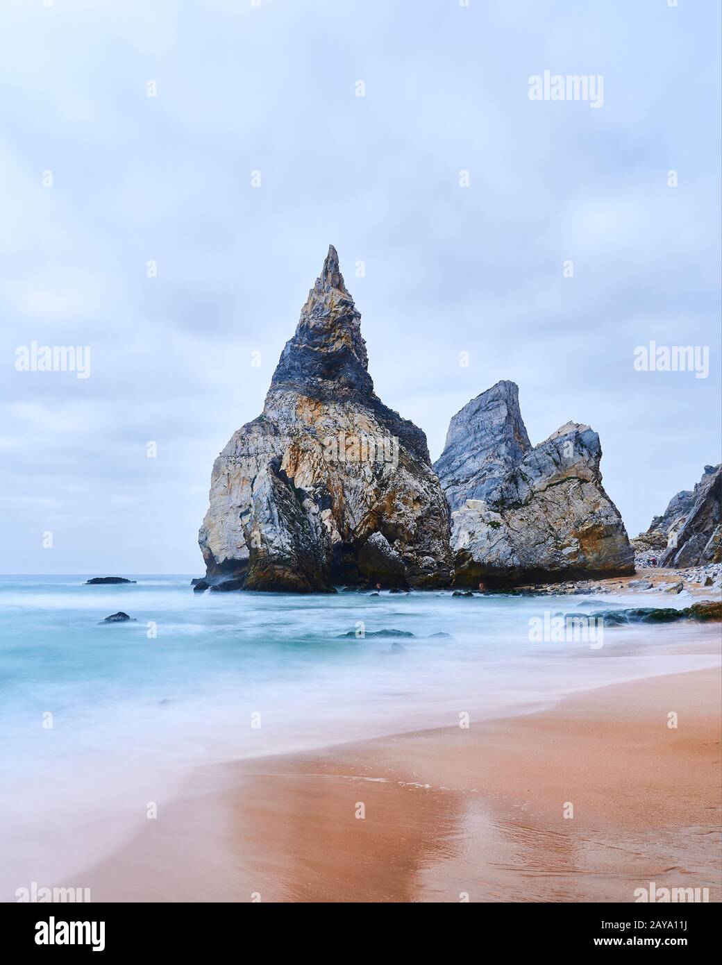 Giant rock at the end of the beach on cloudy day Stock Photo - Alamy