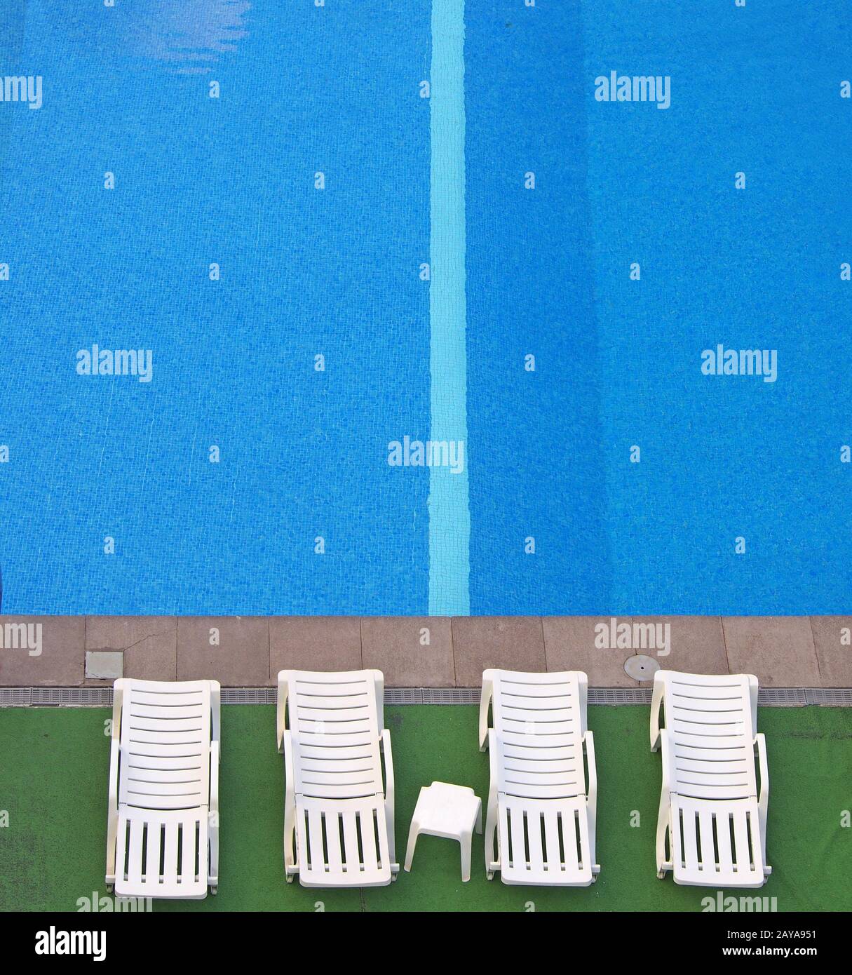 aerial view of white sunbeds at the side of a blue swimming pool with ...