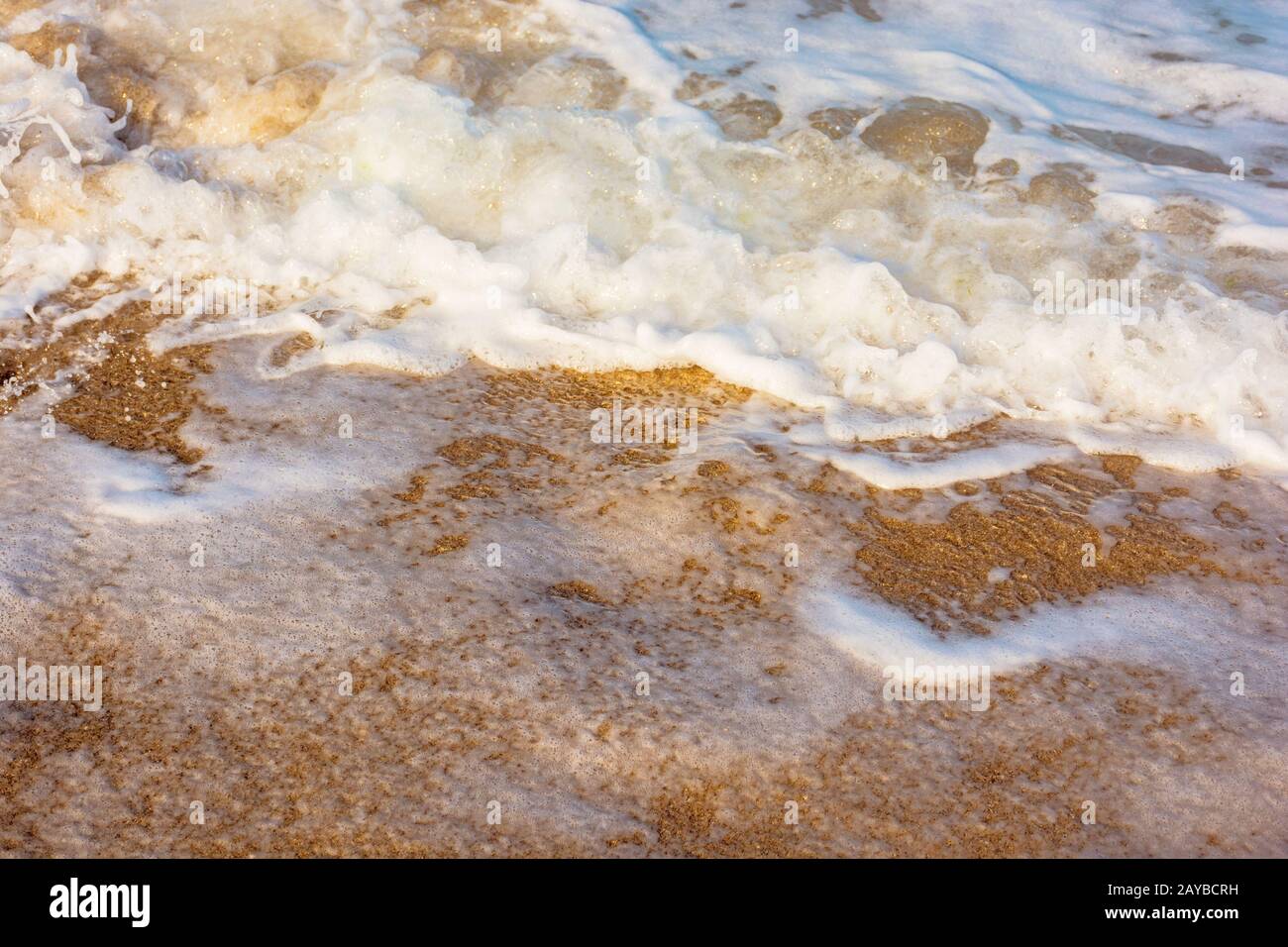sea waves splash foam on the sunny beach. mess of salt water and sand ...