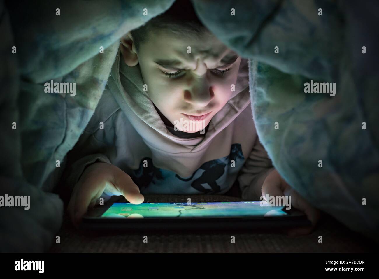 Child watching his tablet in the bed. Illuminated child face from ...