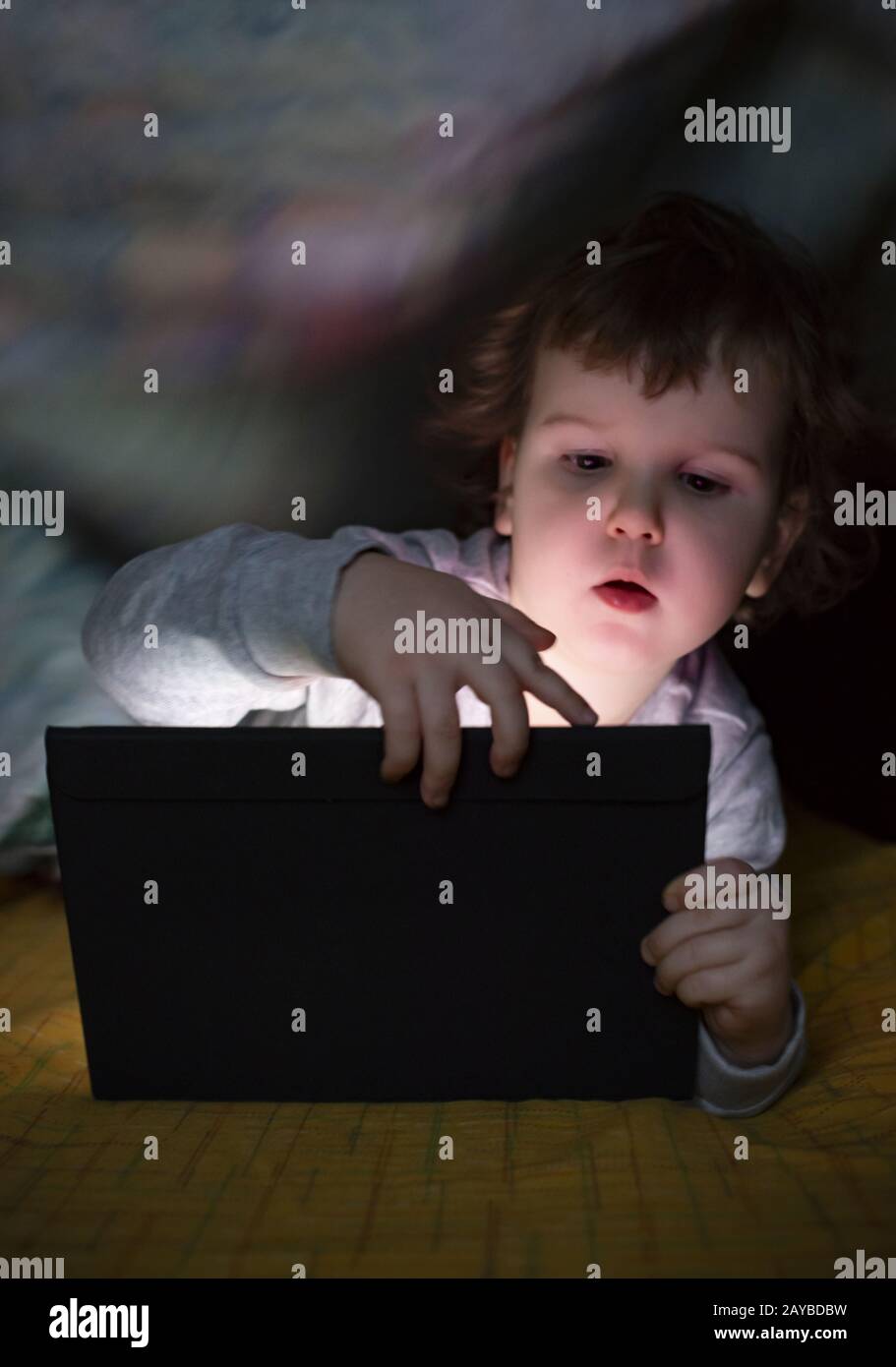 Little girl watching her tablet in the bed. Illuminated child face from ...