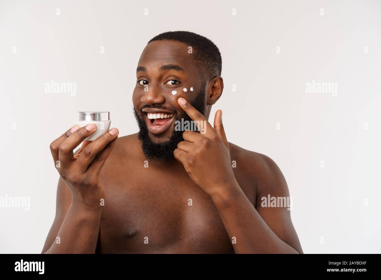 Smiling afro man applying cream on his face. Man's skin care concept ...