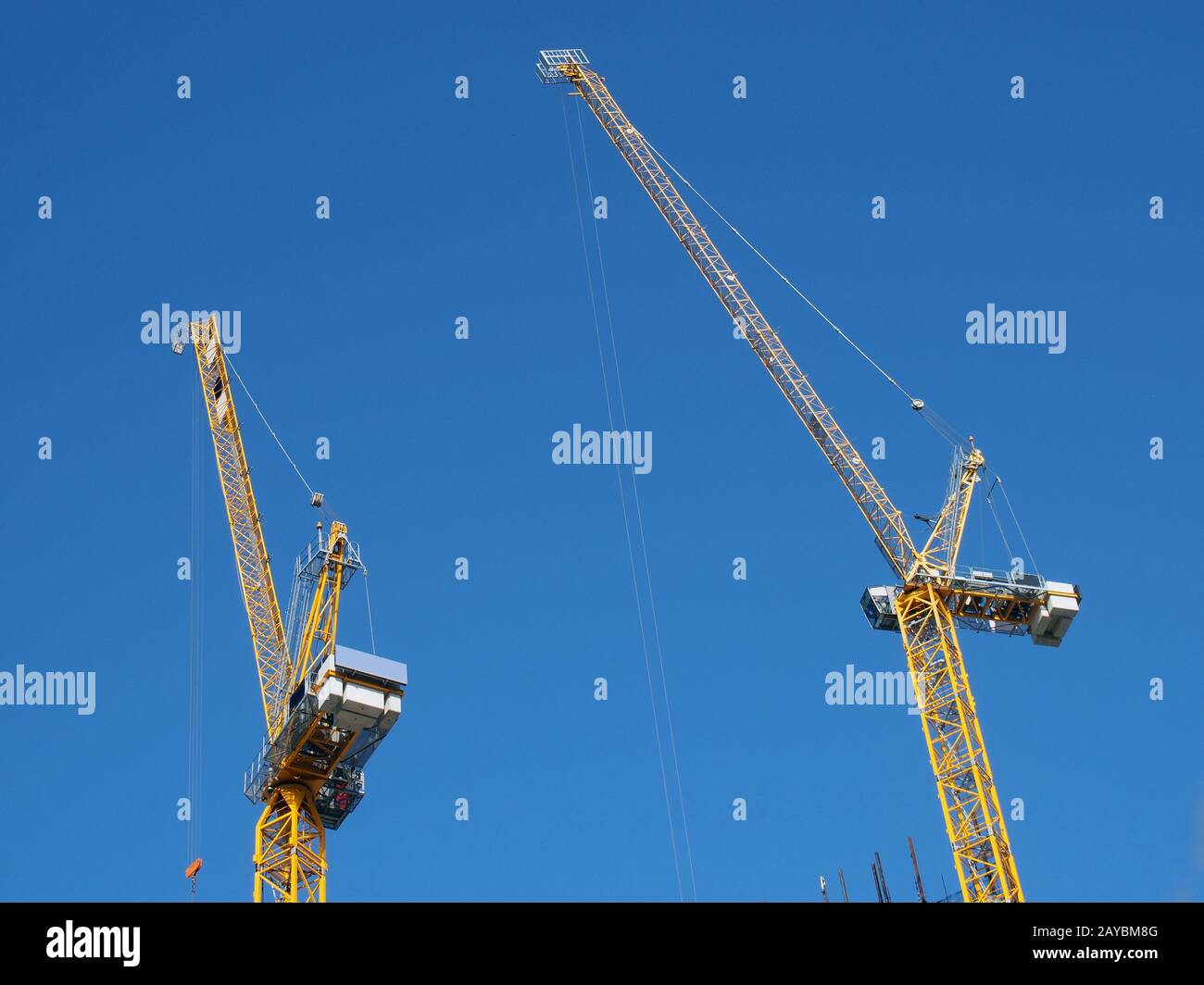 two tall yellow tower cranes working on a construction site against a ...