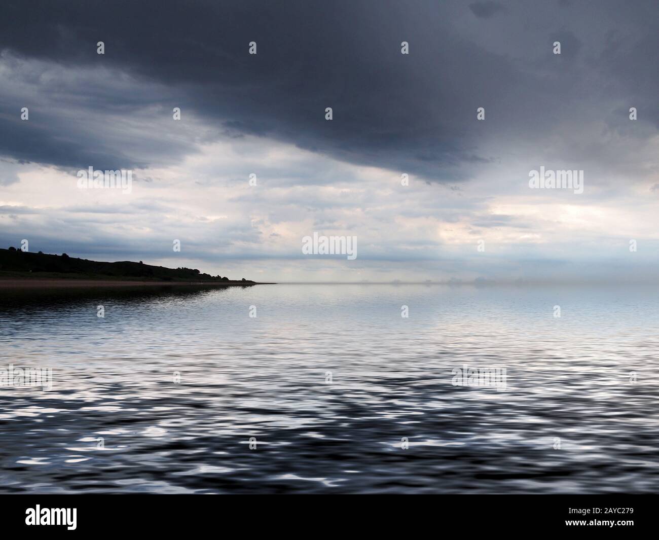 a distant coast reflected in the sea with dramatic dark storm clouds ...