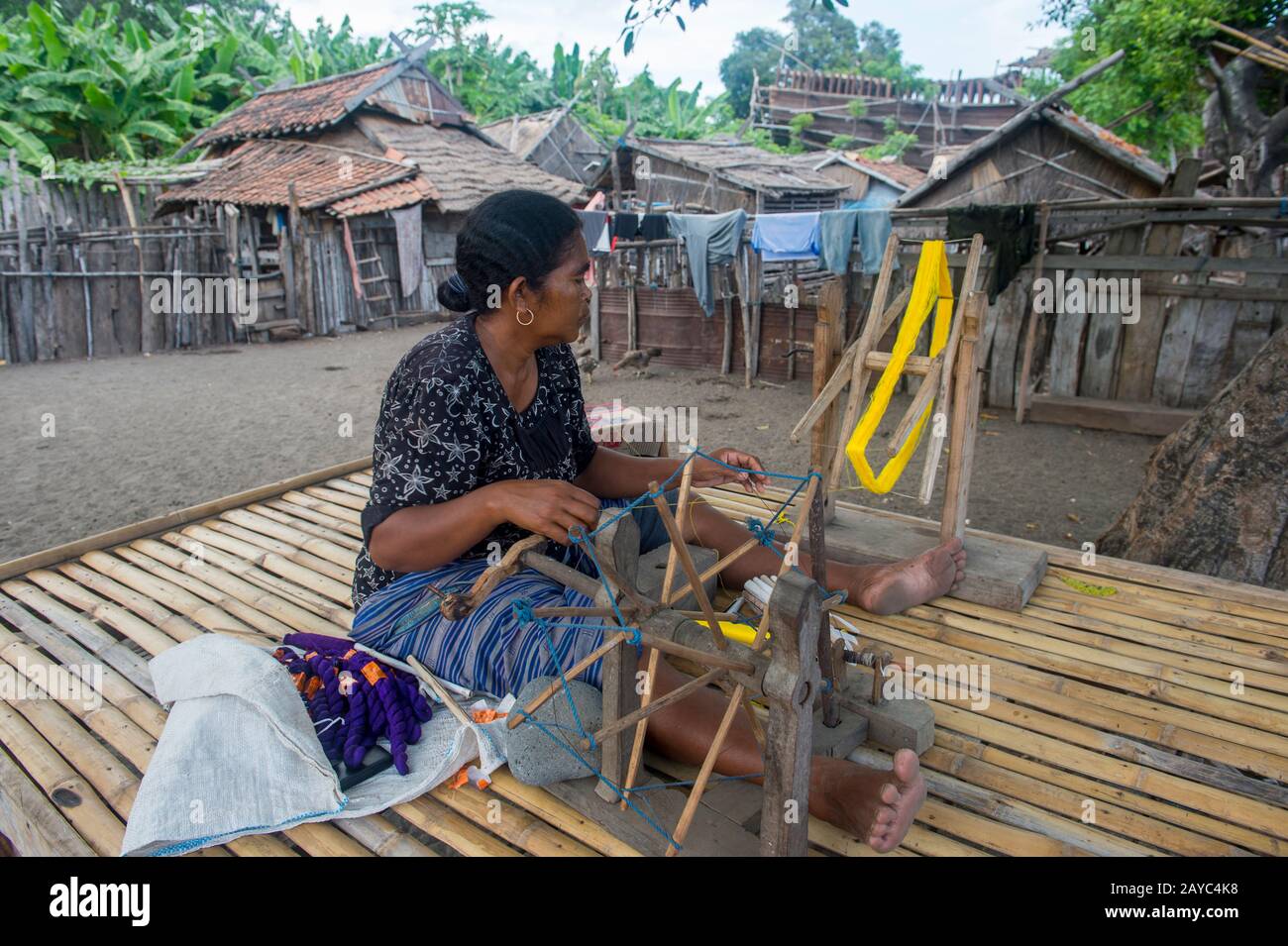 Village scene with a woman spinning yarn in Sangean village, Sangeang ...
