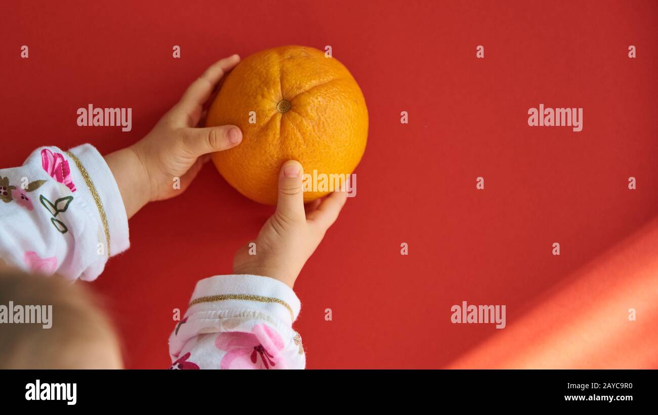 Baby grabbing an orange fruit with both hands Stock Photo - Alamy