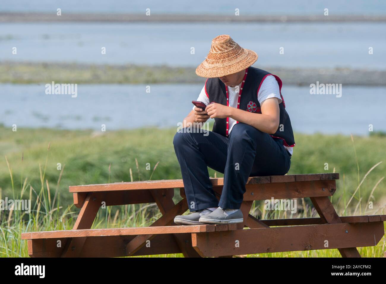 A Tlingit teenage boy with a traditional hat is texting in the village ...