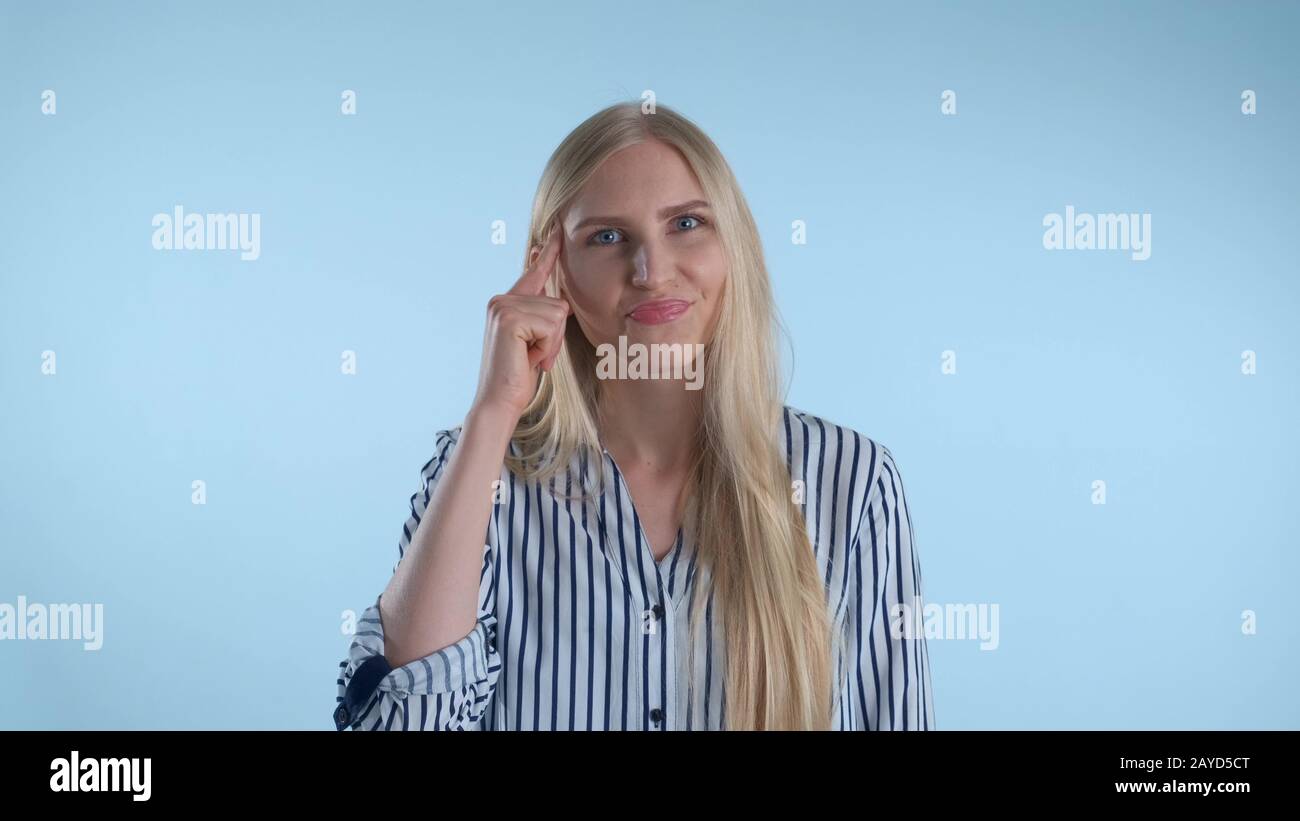 Attractive woman twisting her index finger at temple on blue background ...