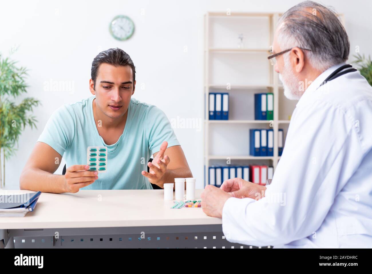 Young man visiting old male doctor Stock Photo - Alamy