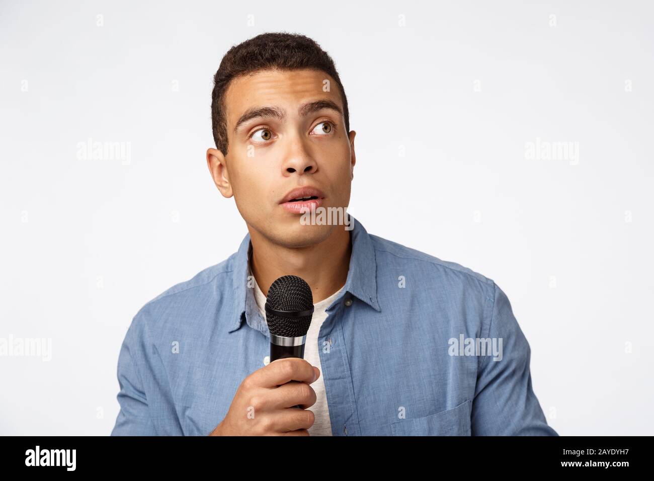 Surprised young man stop speech as hear strange noise, hold microphone ...