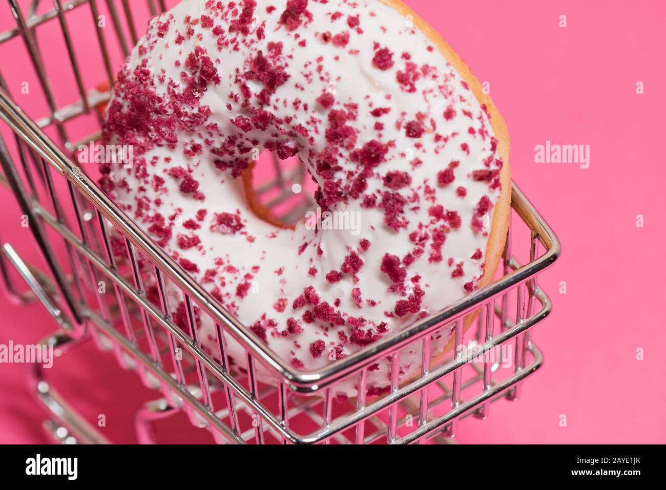 Macro shoot of white donut in shopping trolley over pink background ...