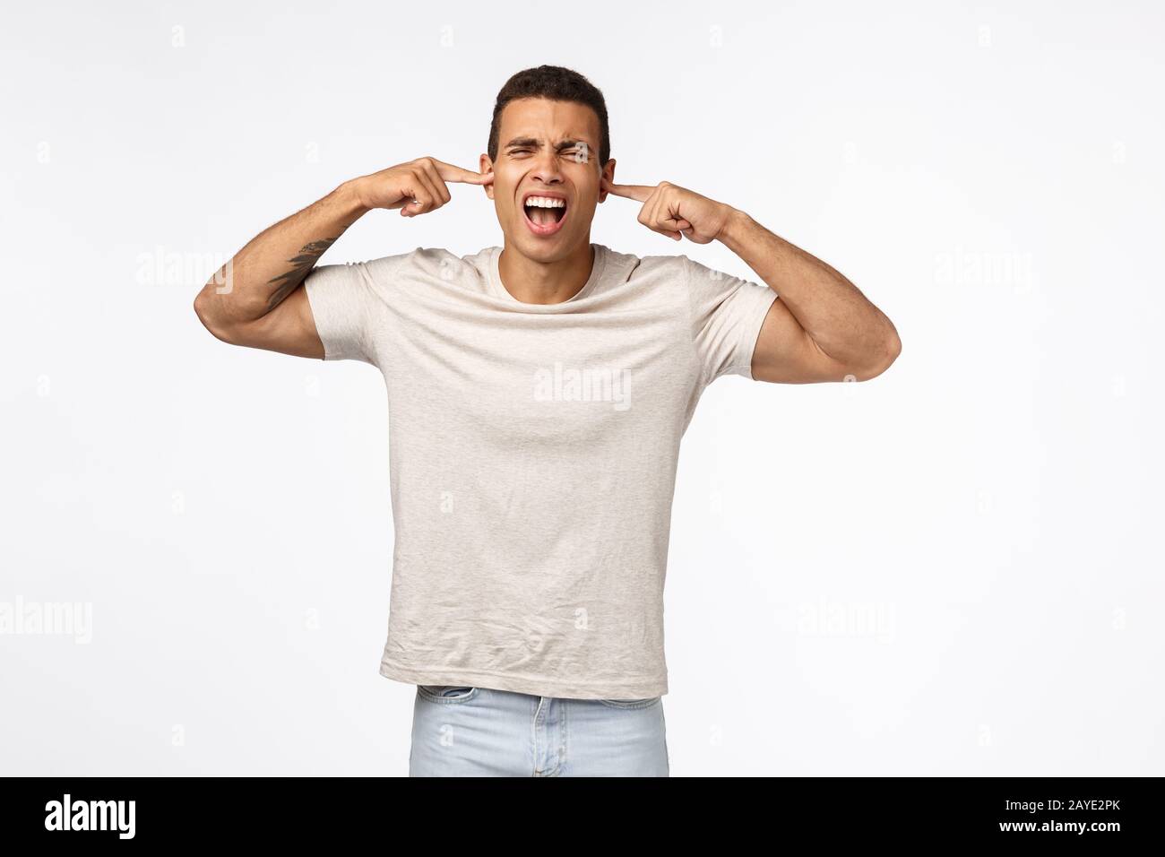 Angry and annoyed athletic young man close ears with fingers, yelling ...