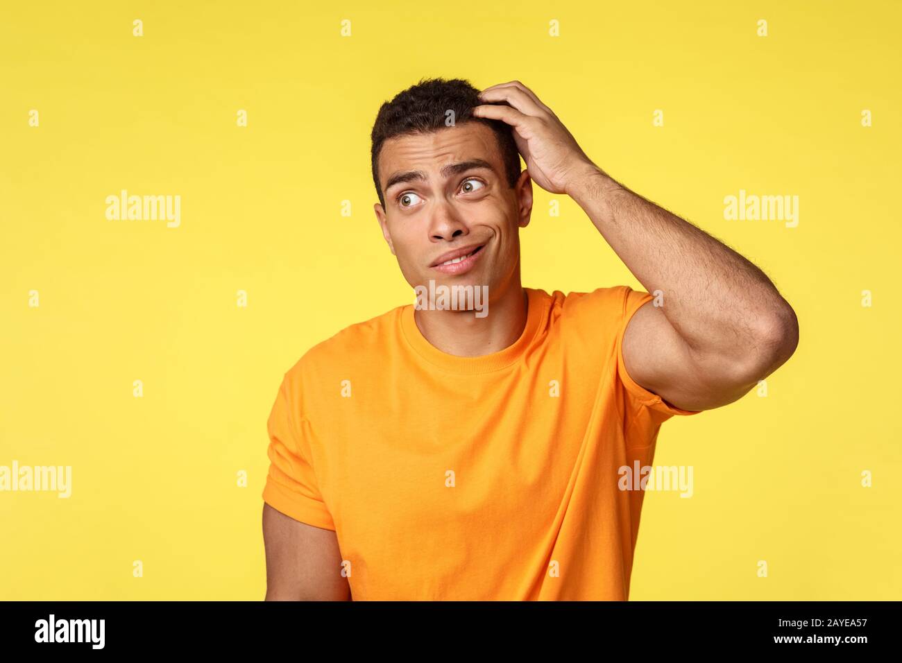 Unsure, clumsy young slightly dumb guy in casual t-shirt, scratching ...