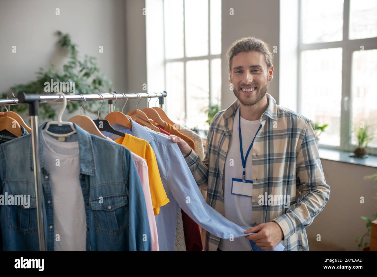 Young man with badge standing near rack with clothes Stock Photo - Alamy