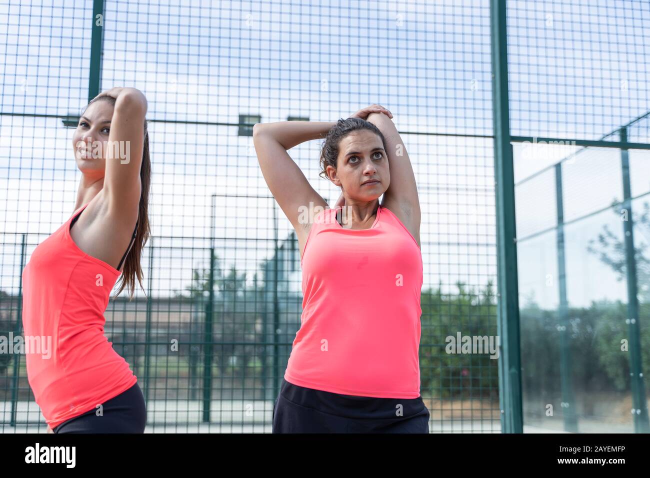 Two girls in sportswear stretching out their arms on an outdoor tennis ...