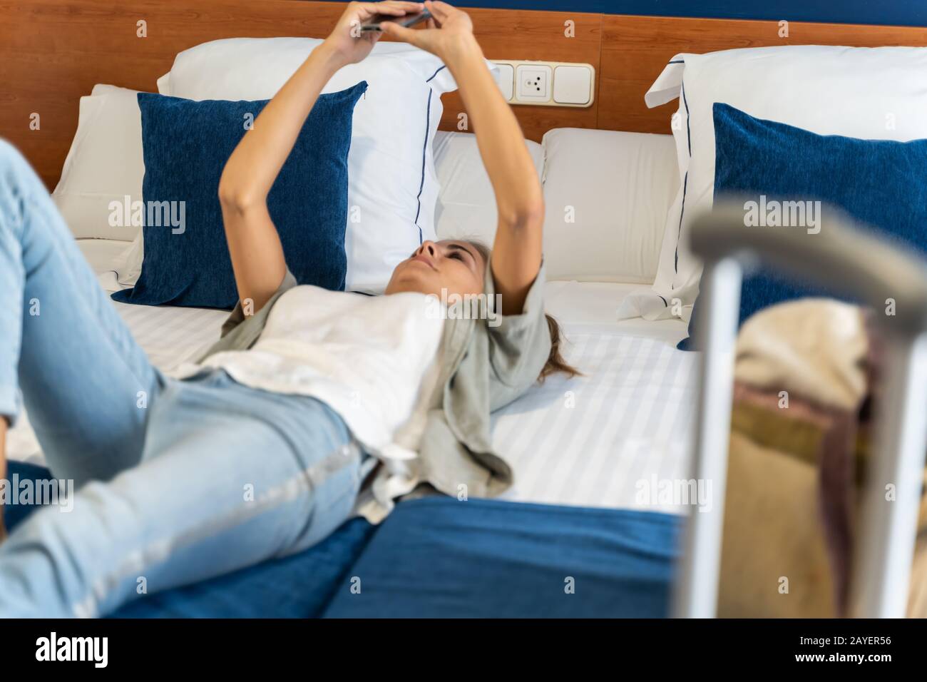 girl looks at the mobile phone stretched out on the hotel bed relaxing ...