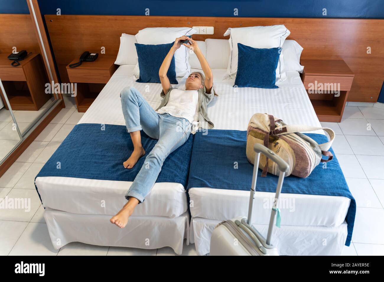girl looks at the mobile phone stretched out on the hotel bed relaxing ...